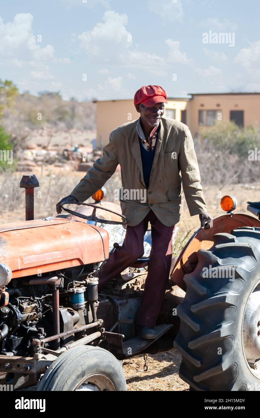 Old African farmer climbing on his tractor at the farm in the village ...