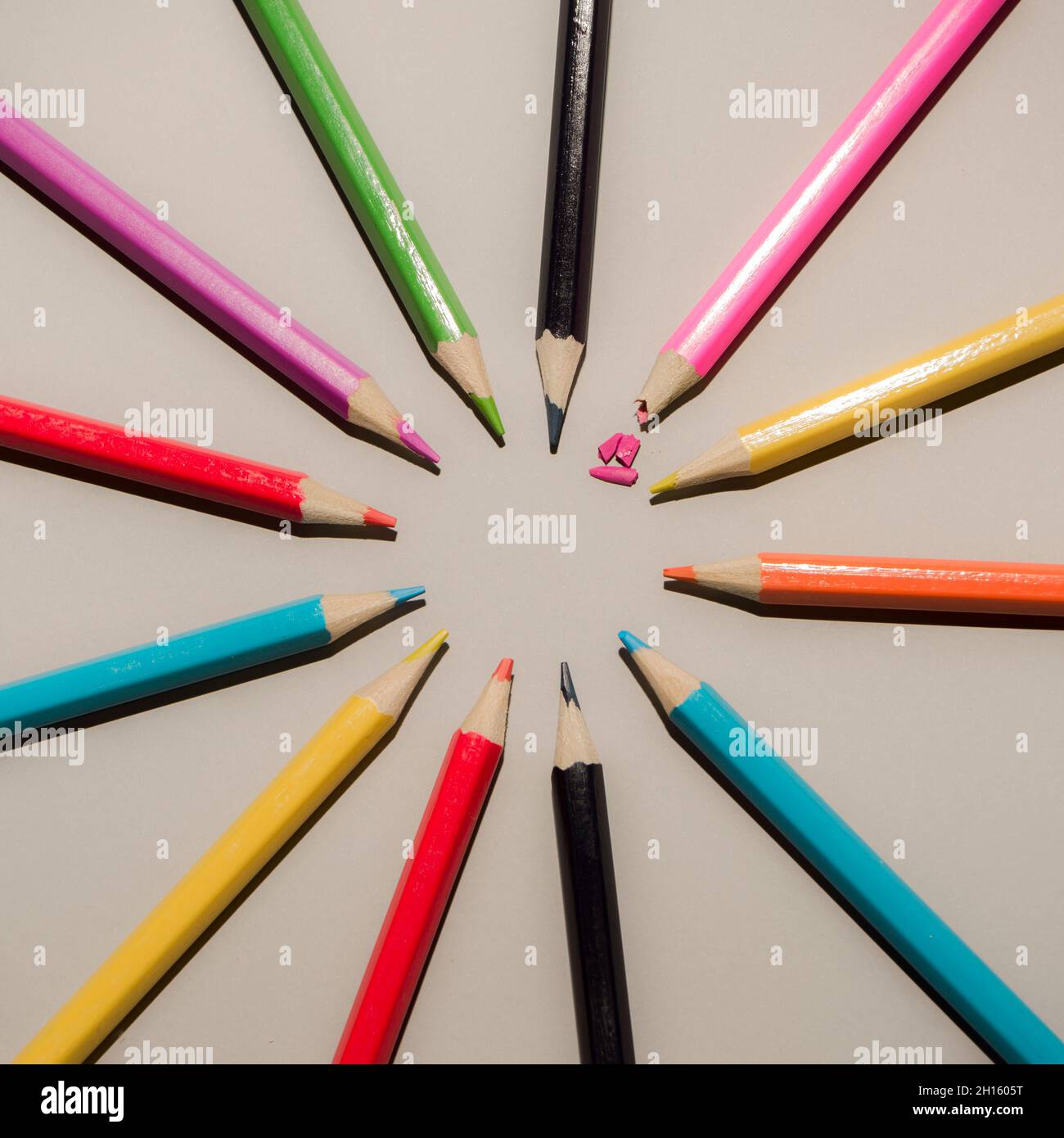 Colored pencils top view circle layout on grey background. Crushed pink ...