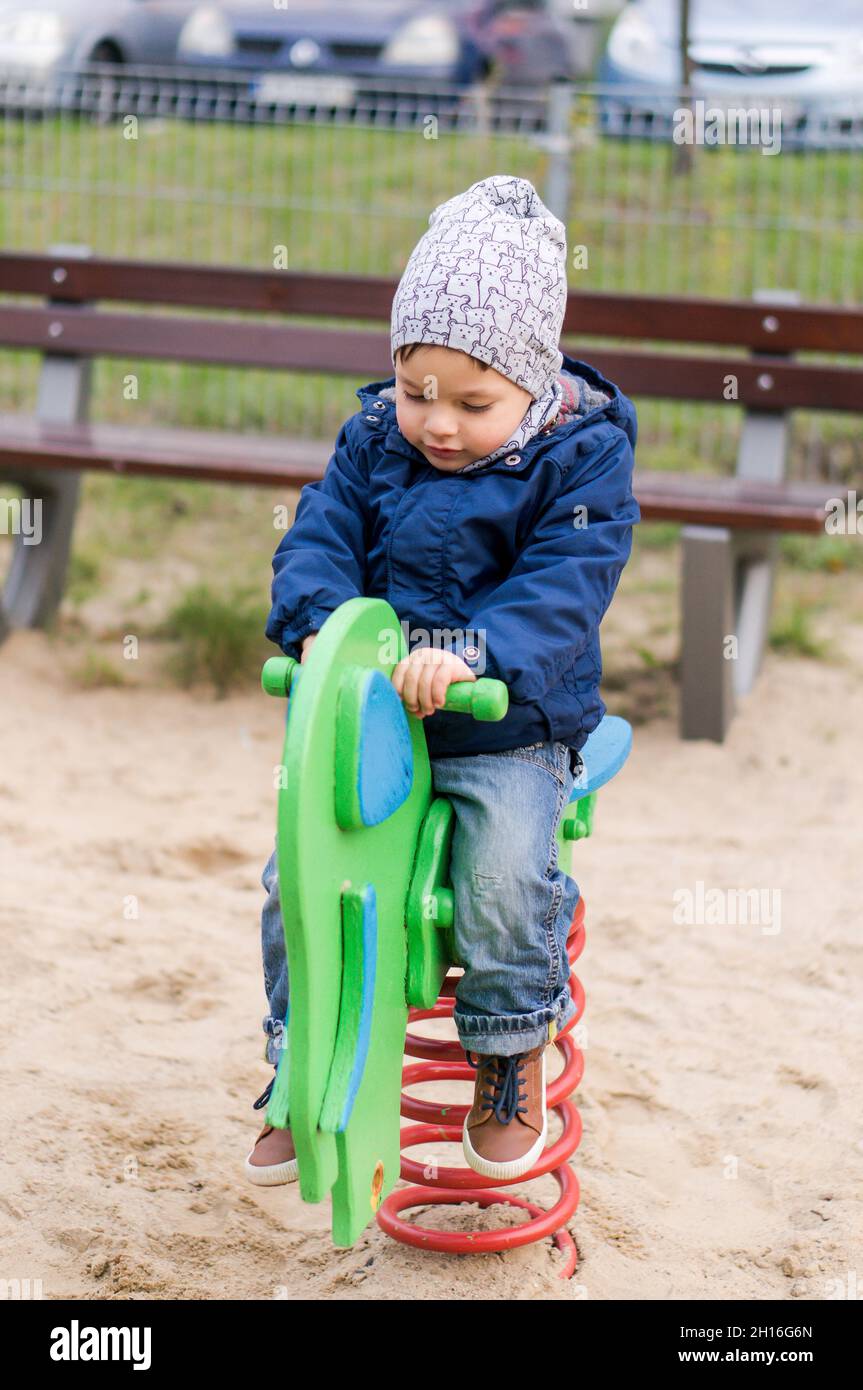 A Caucasian male kid sitting on a green spring swing at the park Stock ...