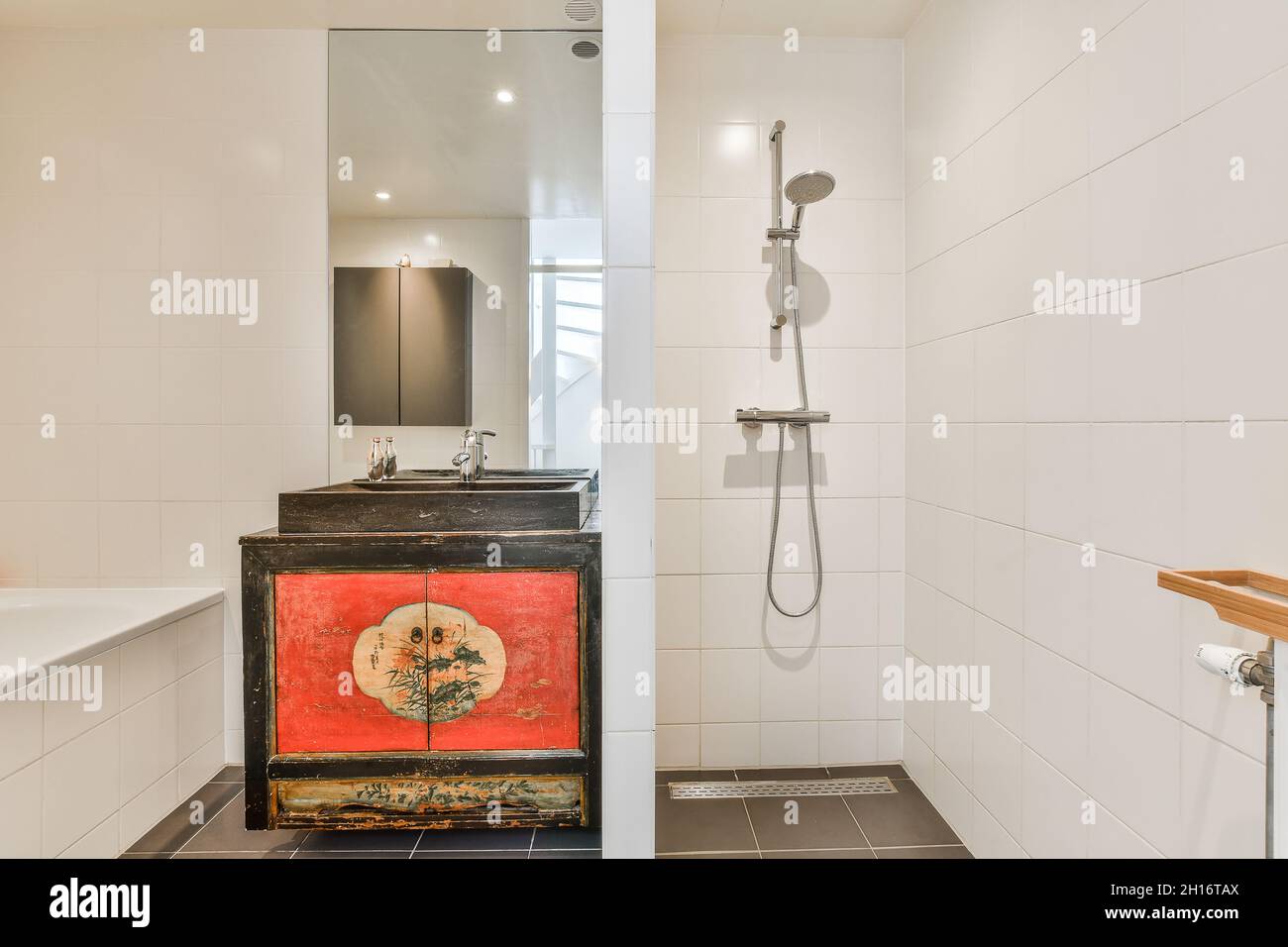 Tub near cabinet with sink at tiled wall with mirror with reflection in ...