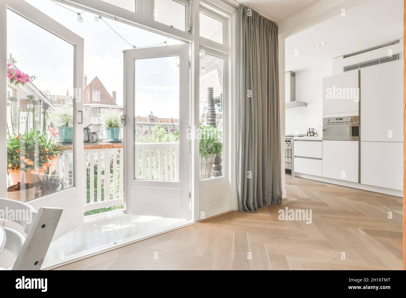 Balcony opened windows in spacious kitchen with white furniture and modern appliances in light ...