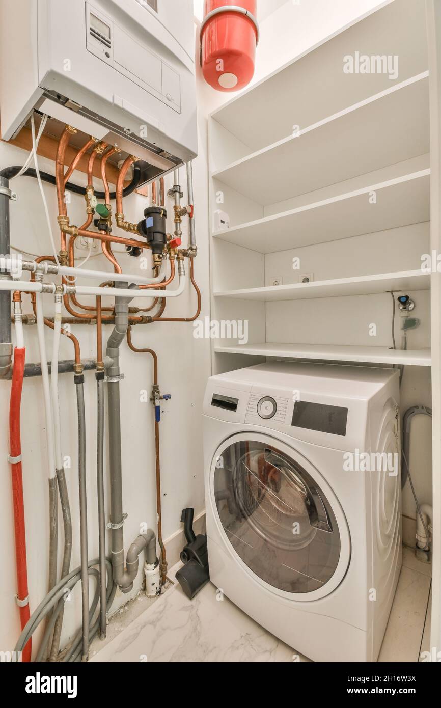 Modern washing machine and water heater with various hoses in bathroom ...