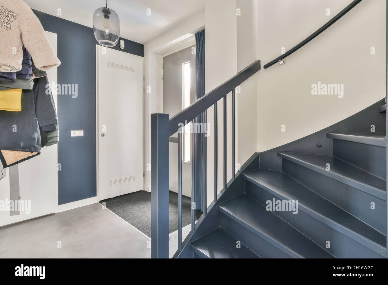 Blue stairway with banister located near doors and outerwear in sunlit ...