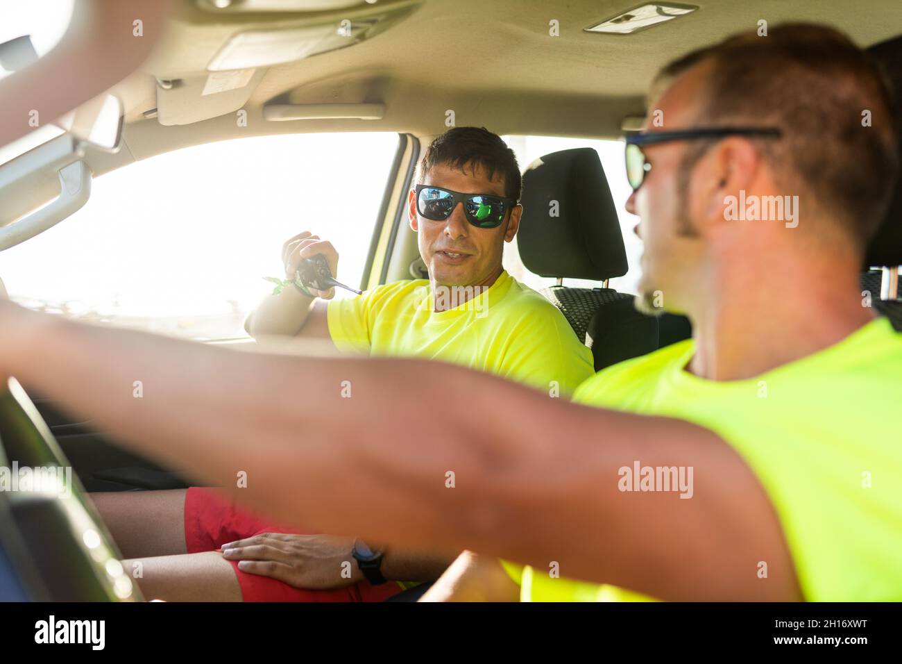 Side view of lifeguard in sunglasses driving car near male talking on ...