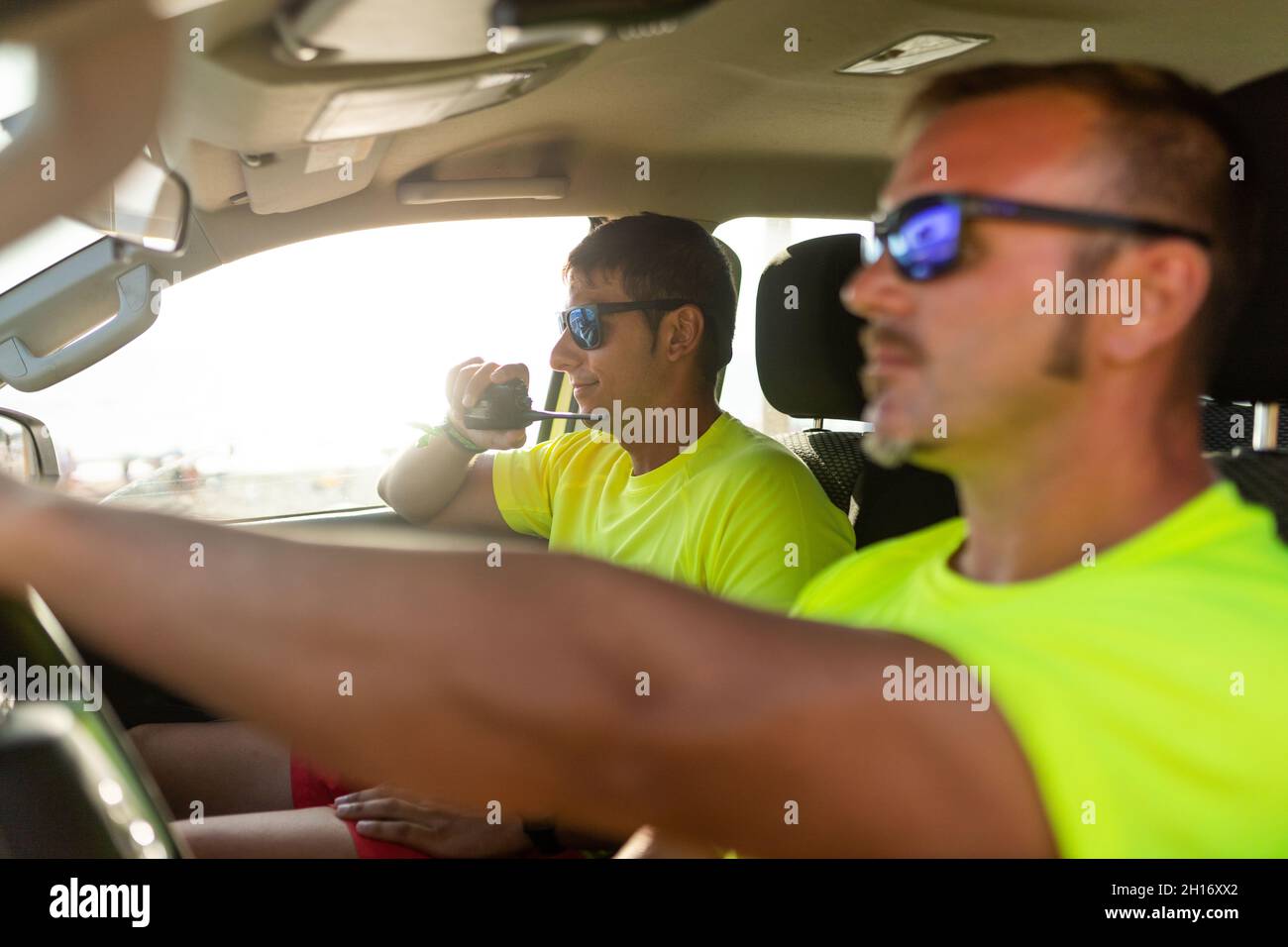 Side view of lifeguard in sunglasses driving car near male talking on ...