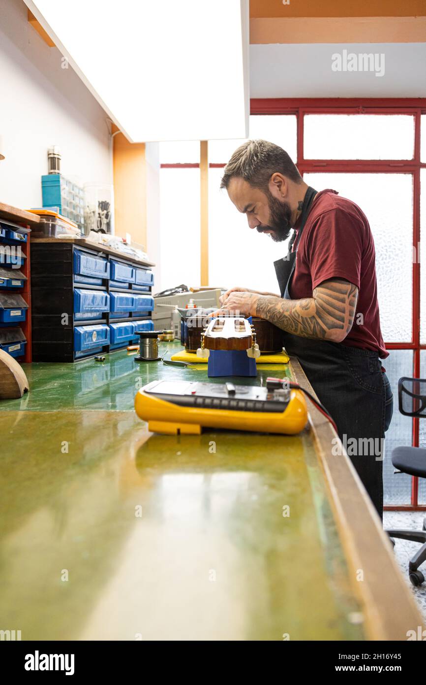 Side view of serious adult male master fixing guitar at table near ...