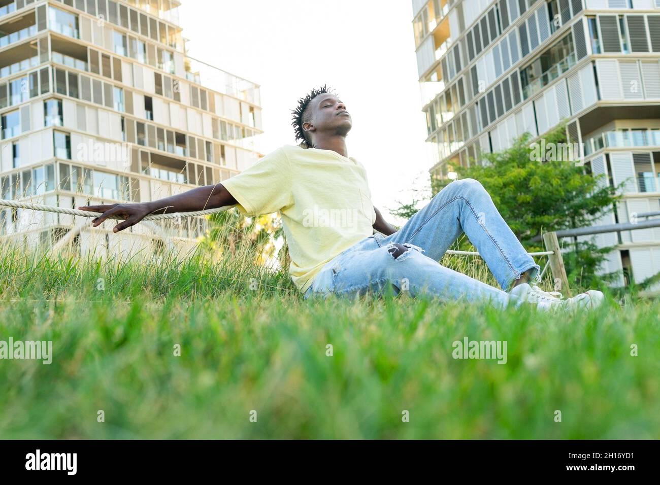 Young African American male in casual clothes sitting on grass with ...