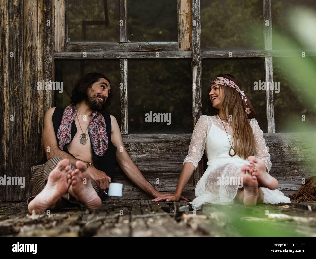 Hippie couple sitting on the porch floor looking at each other while ...