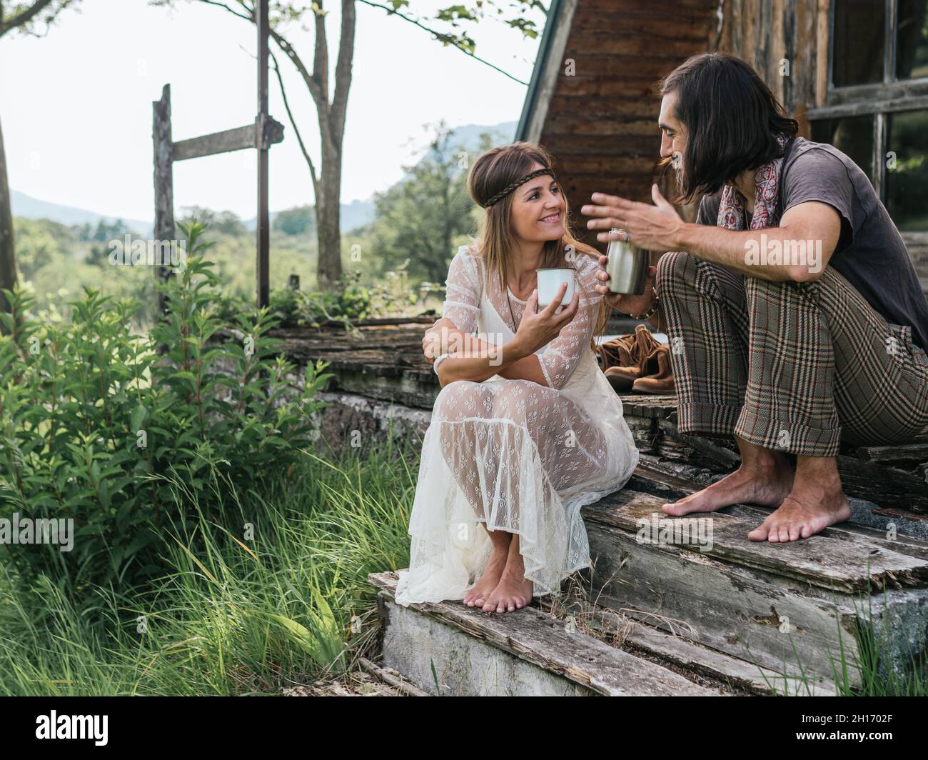 Barefoot hippie couple sharing a coffee while talking and looking at each other on a wooden ...