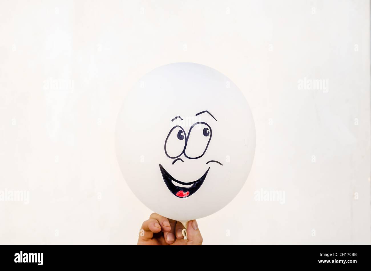 Positive white balloon with a laughing painted face against a light ...