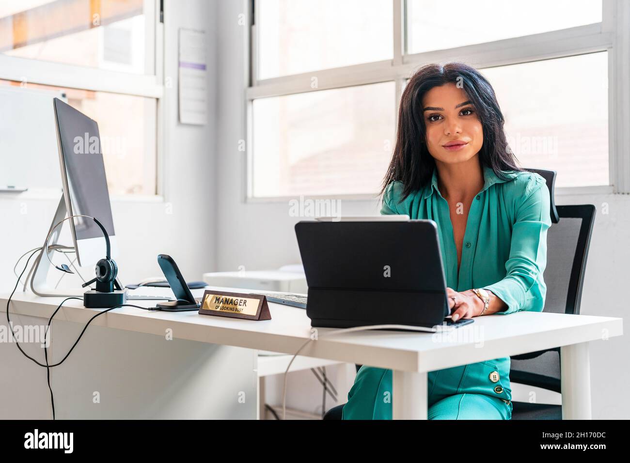 Elegant female employee in formal wear looking at camera while sitting ...