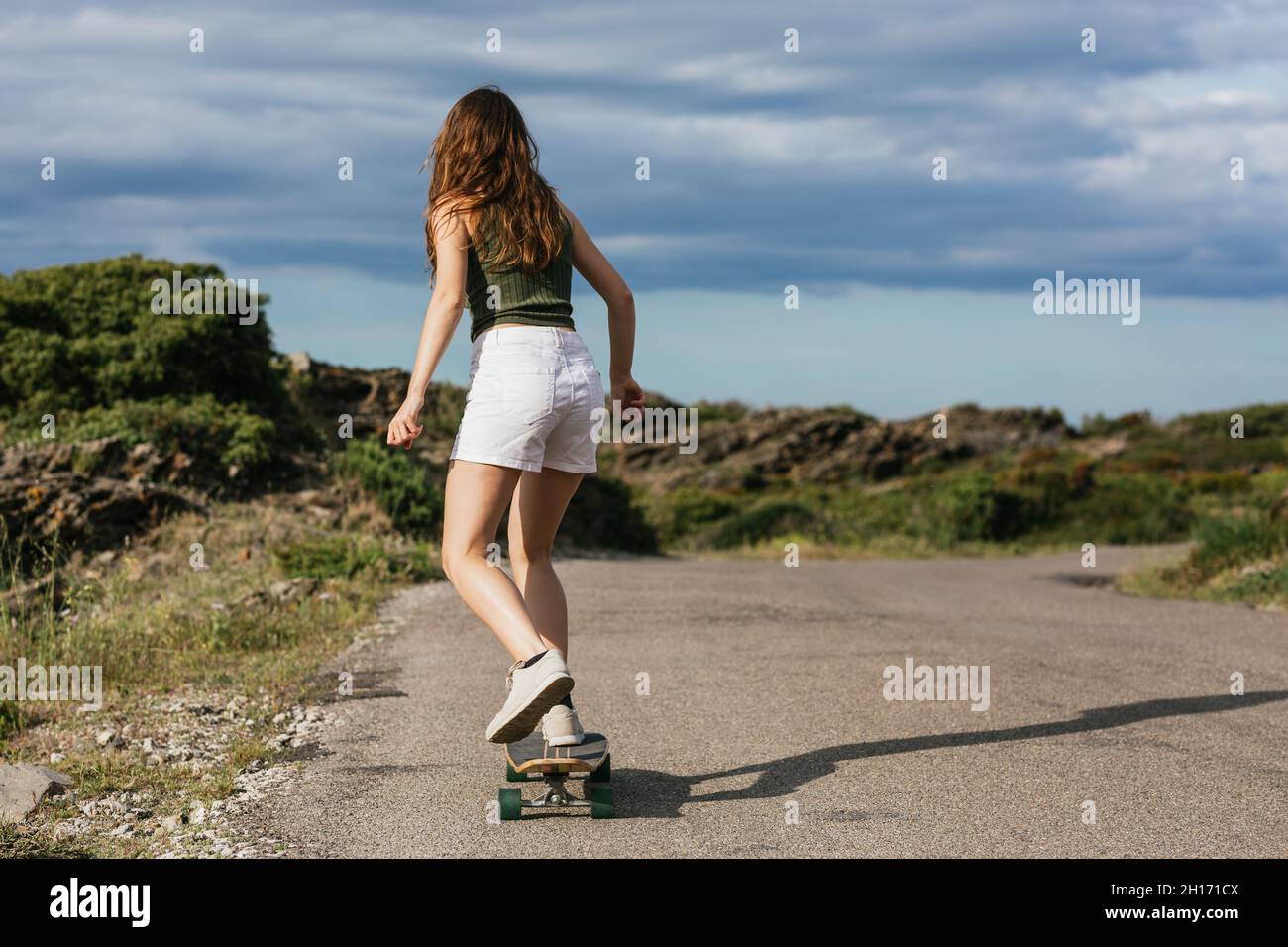 Full body back view of unrecognizable young female riding longboard on ...