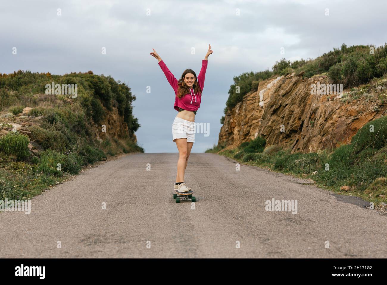 Full body of happy female raising hands while riding longboard on ...