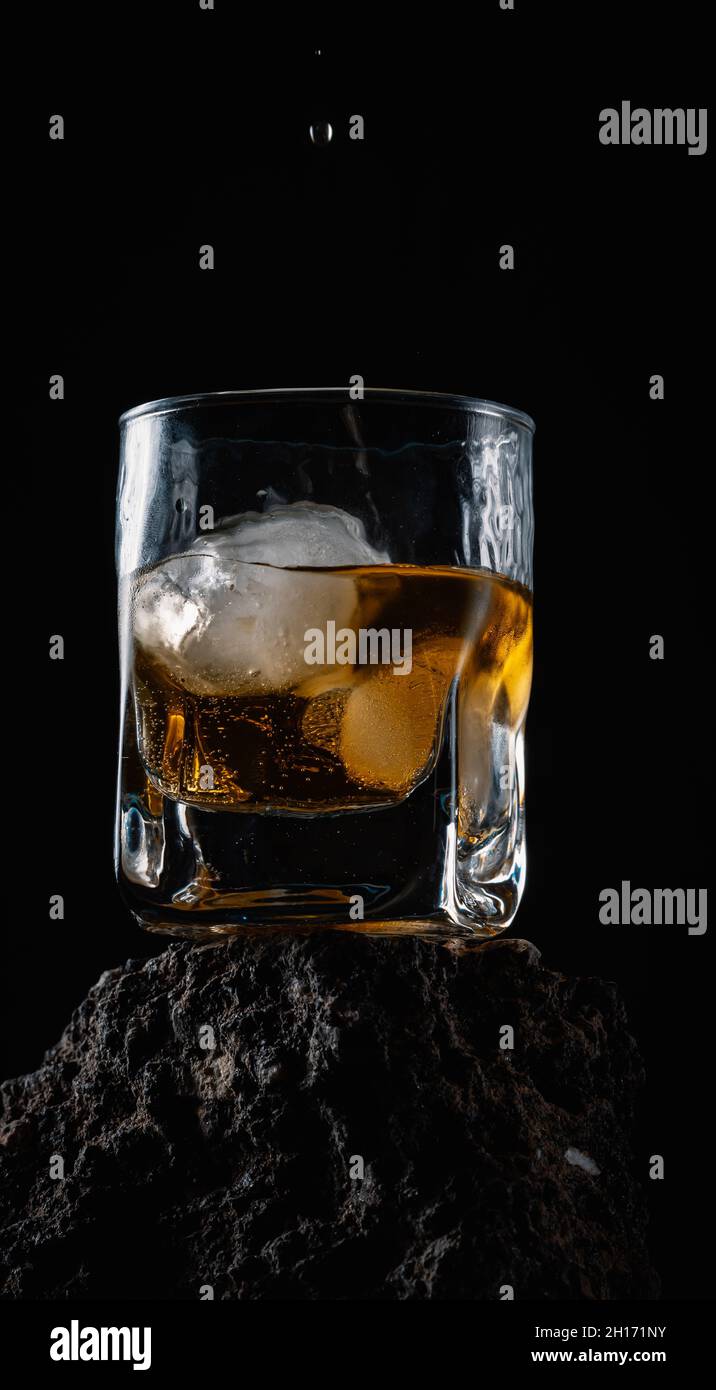 Whiskey drops falling on ice cubes served in crystal glass placed on ...