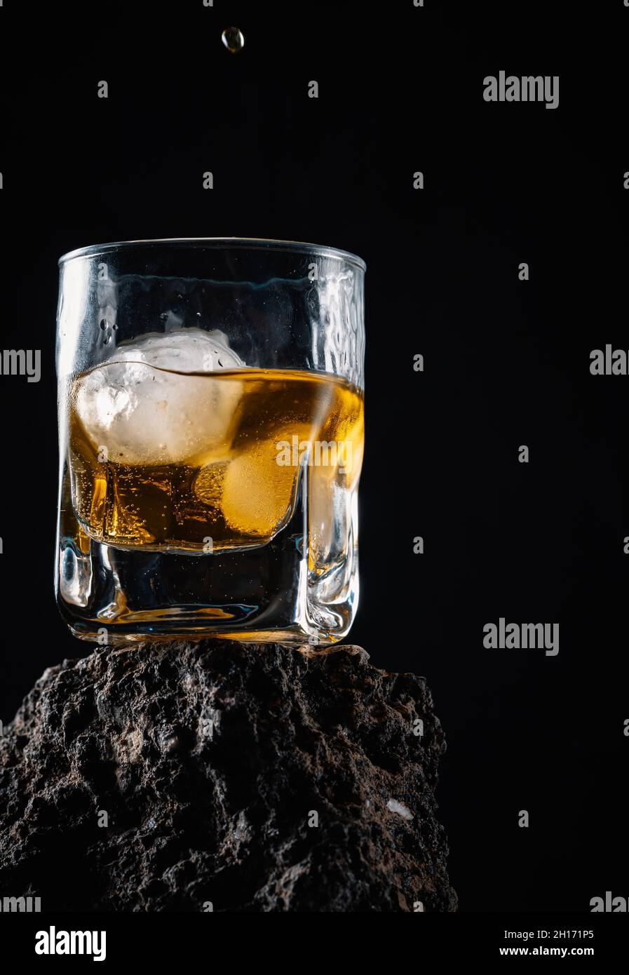 Whiskey drops falling on ice cubes served in crystal glass placed on ...