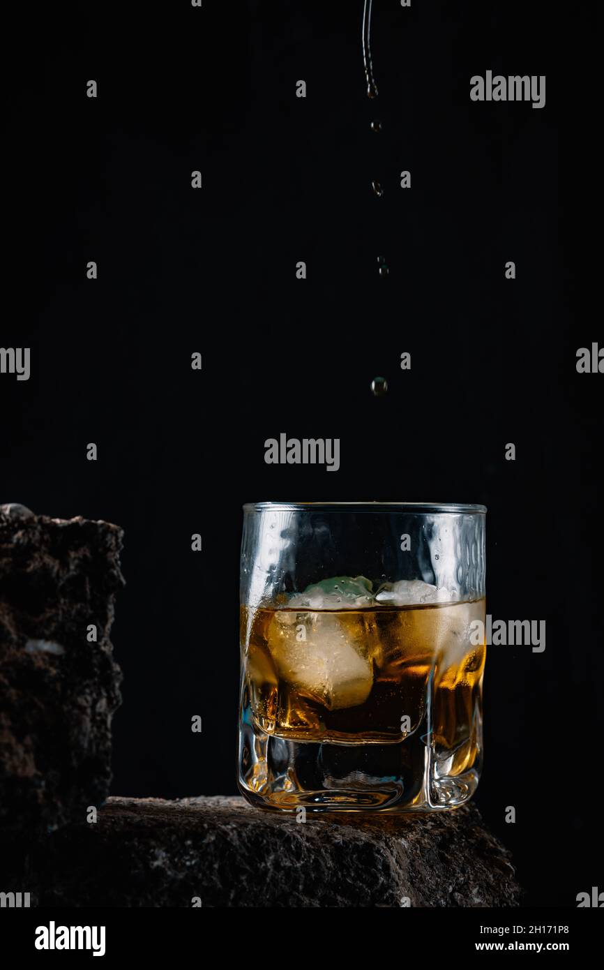 Whiskey drops falling on ice cubes served in crystal glass placed on ...