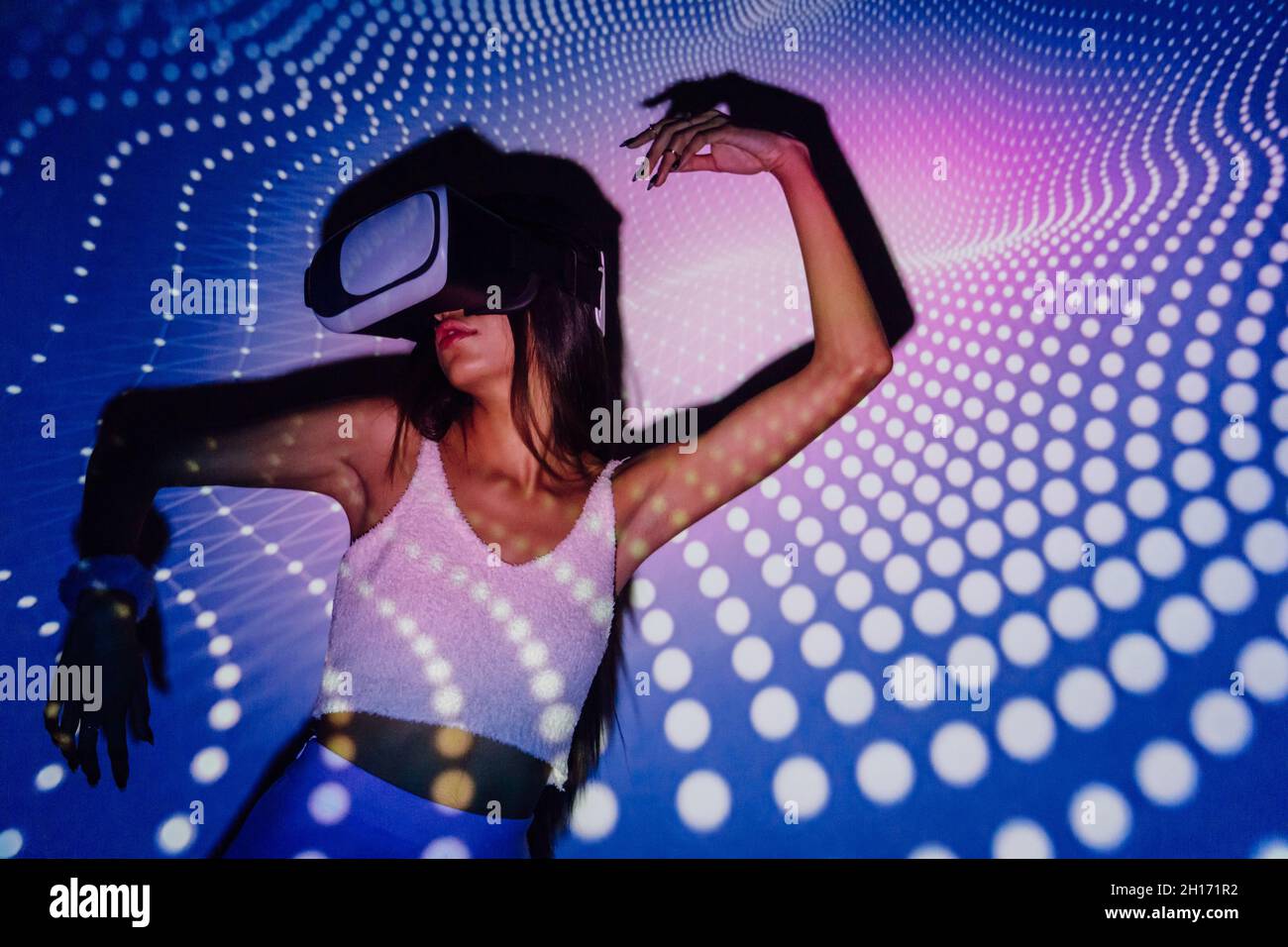 Trendy female in crop top experiencing virtual reality in headset while ...