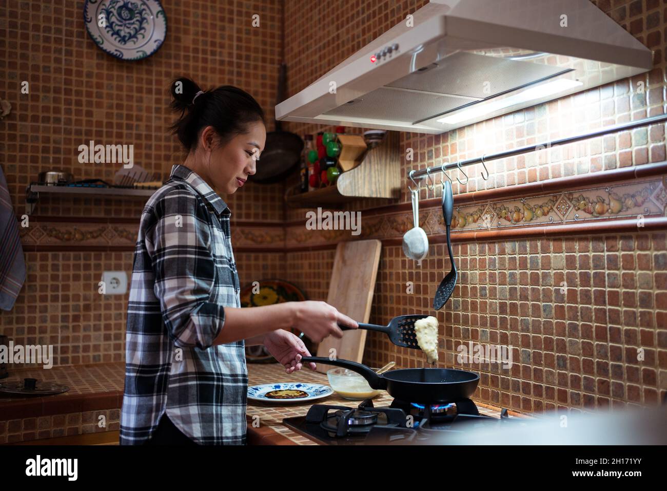 Side view of focused young Asian female in casual clothes cooking yummy ...
