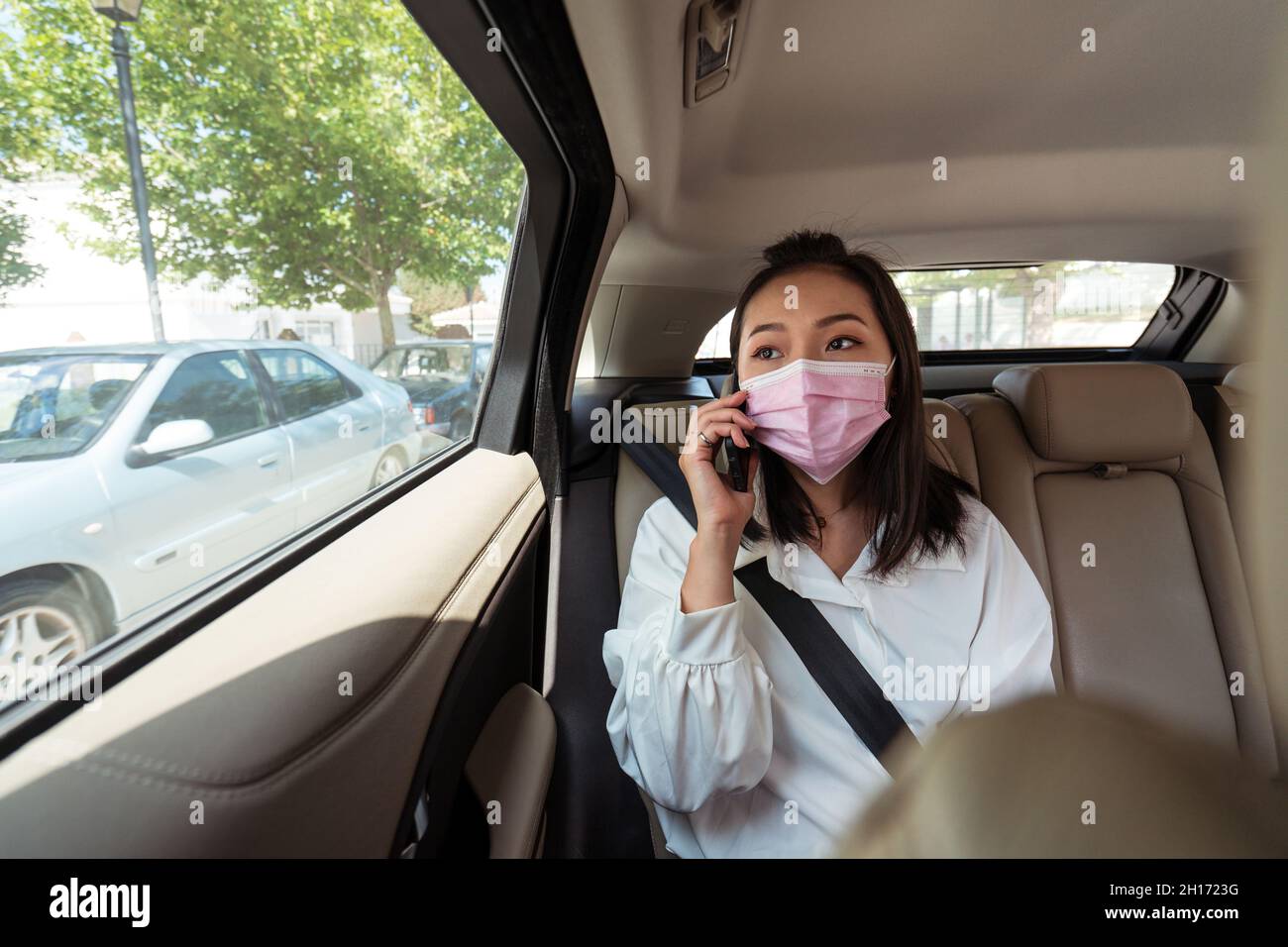 Ethnic female passenger in protective mask sitting with fasten seat ...