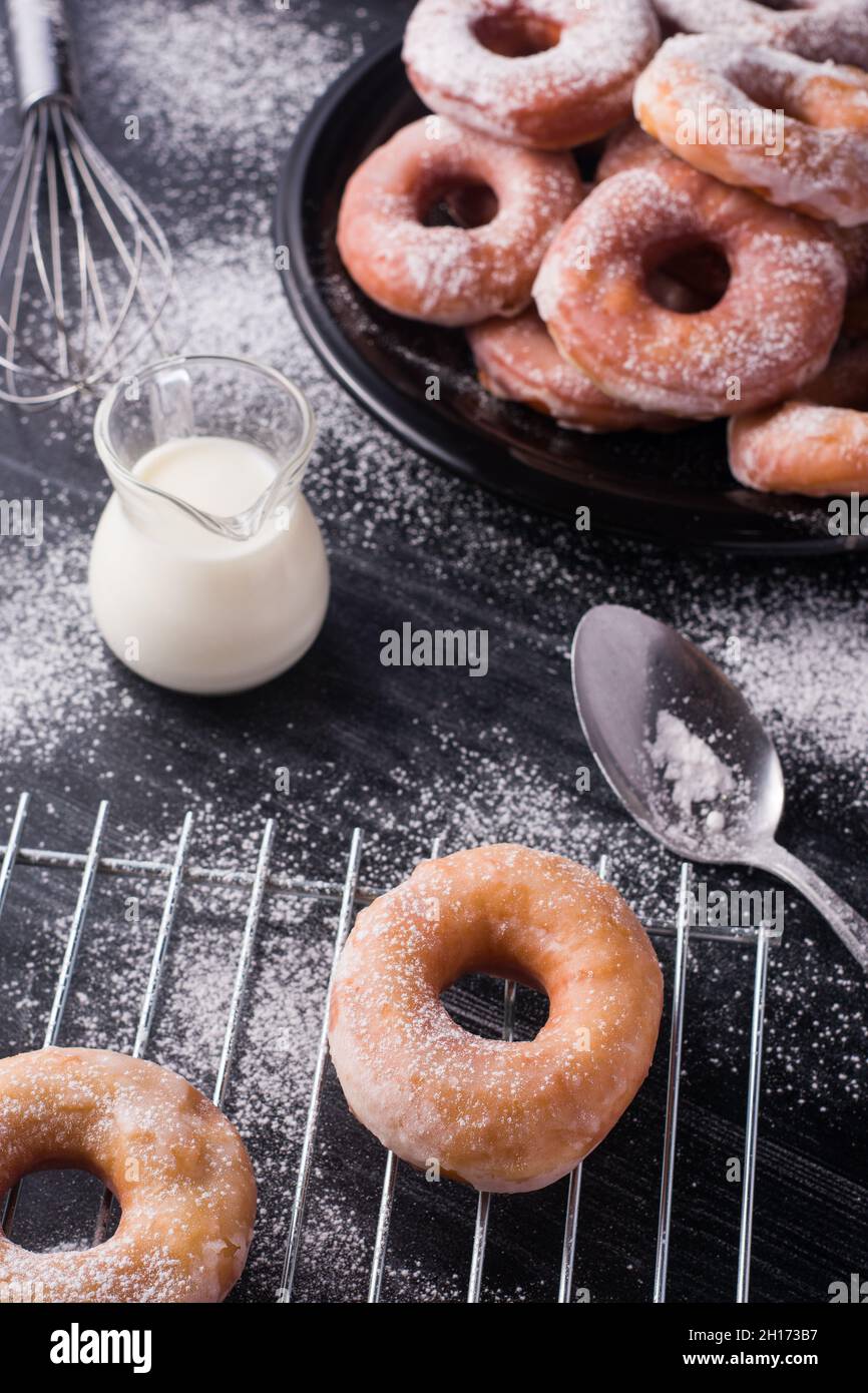 Sweet fried doughnuts served on plate near metal cooling rack and jug of milk on black messy ...