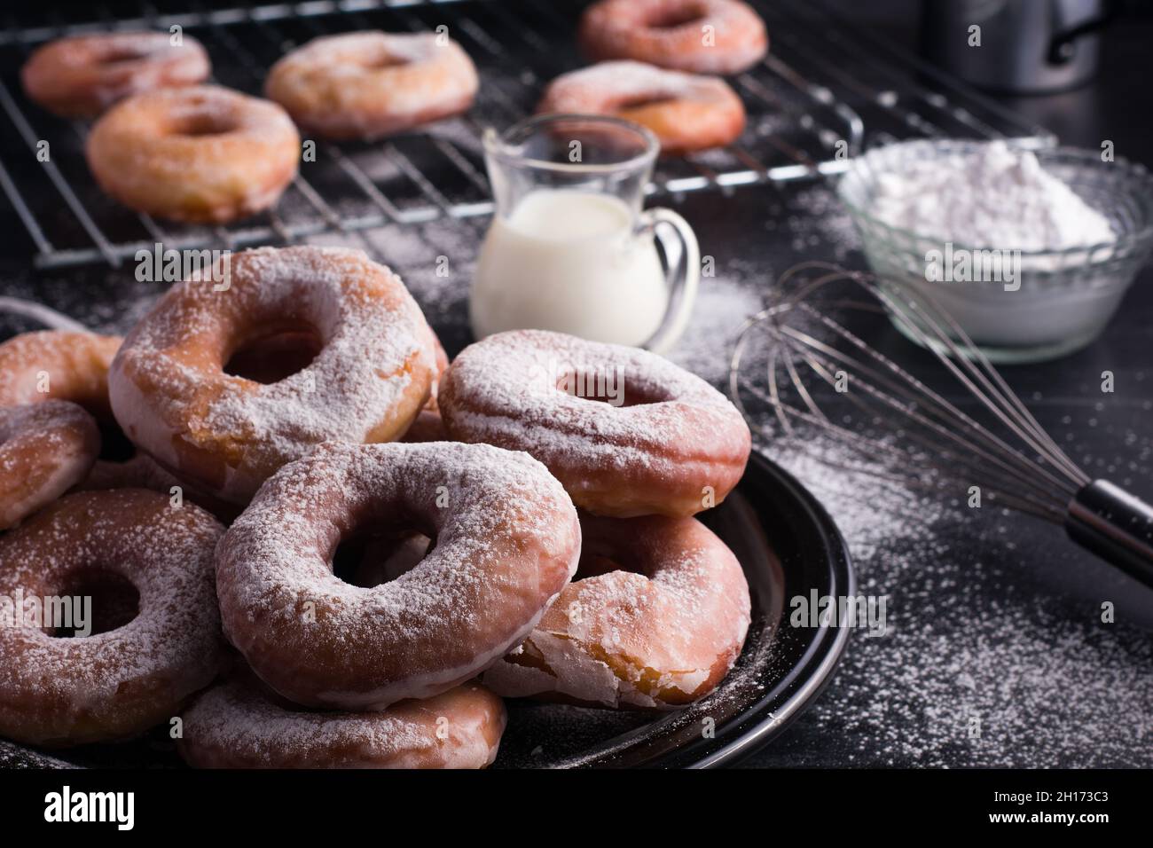 Sweet fried doughnuts served on plate near metal cooling rack and jug of milk on black messy ...