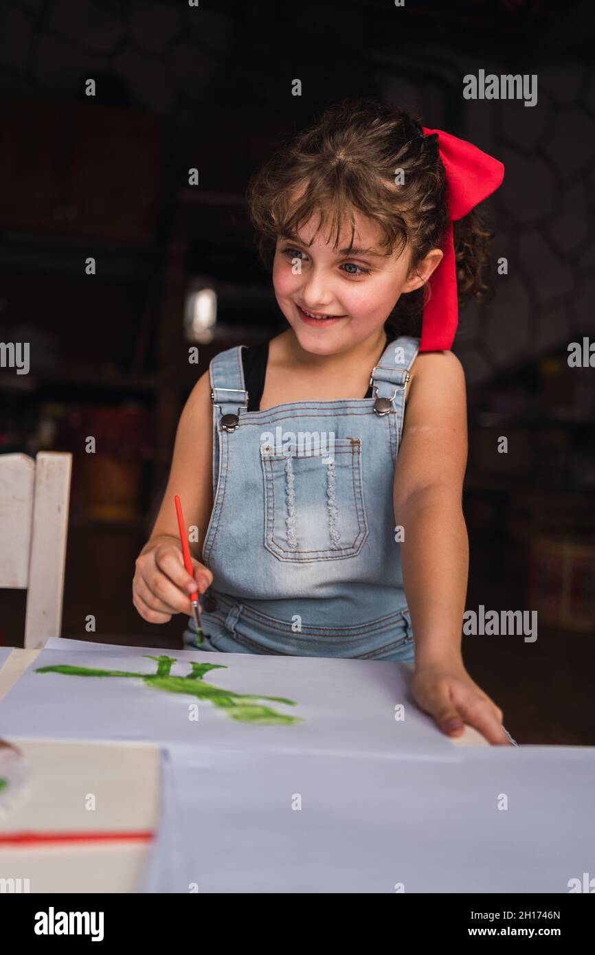 Positive girl in denim overall with paintbrush painting with green ...