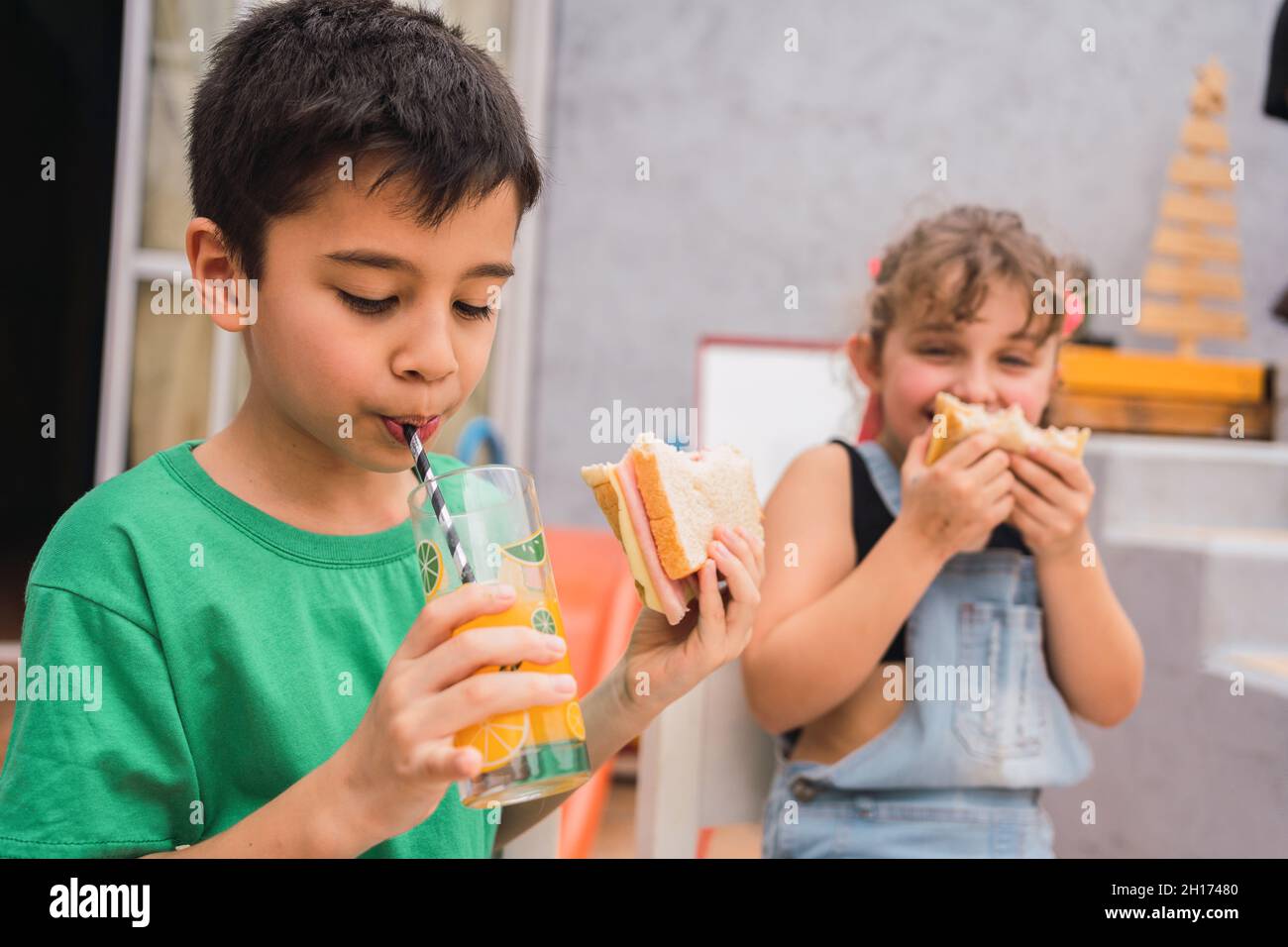 Cheerful children laughing and eating fresh sandwiches while sitting at ...