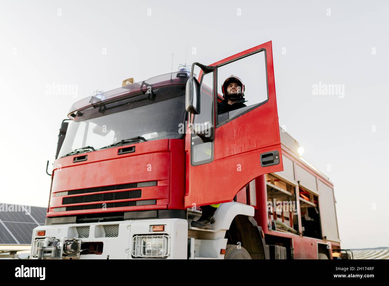 Firefighter driver wearing protective uniform climbing up fire truck ...