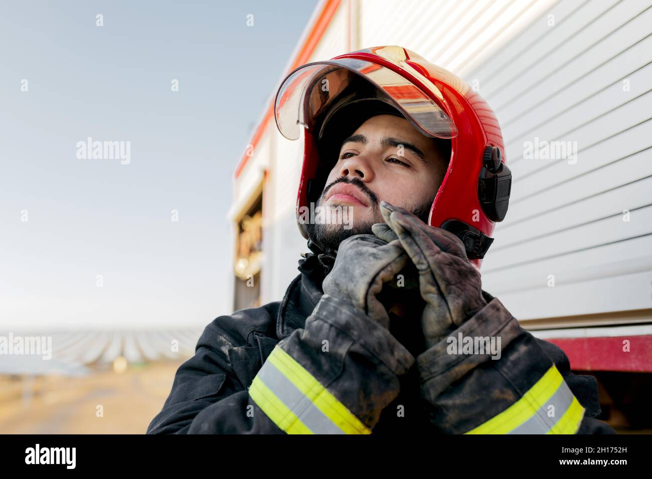Young bearded male fireman wearing uniform with protective gloves ...