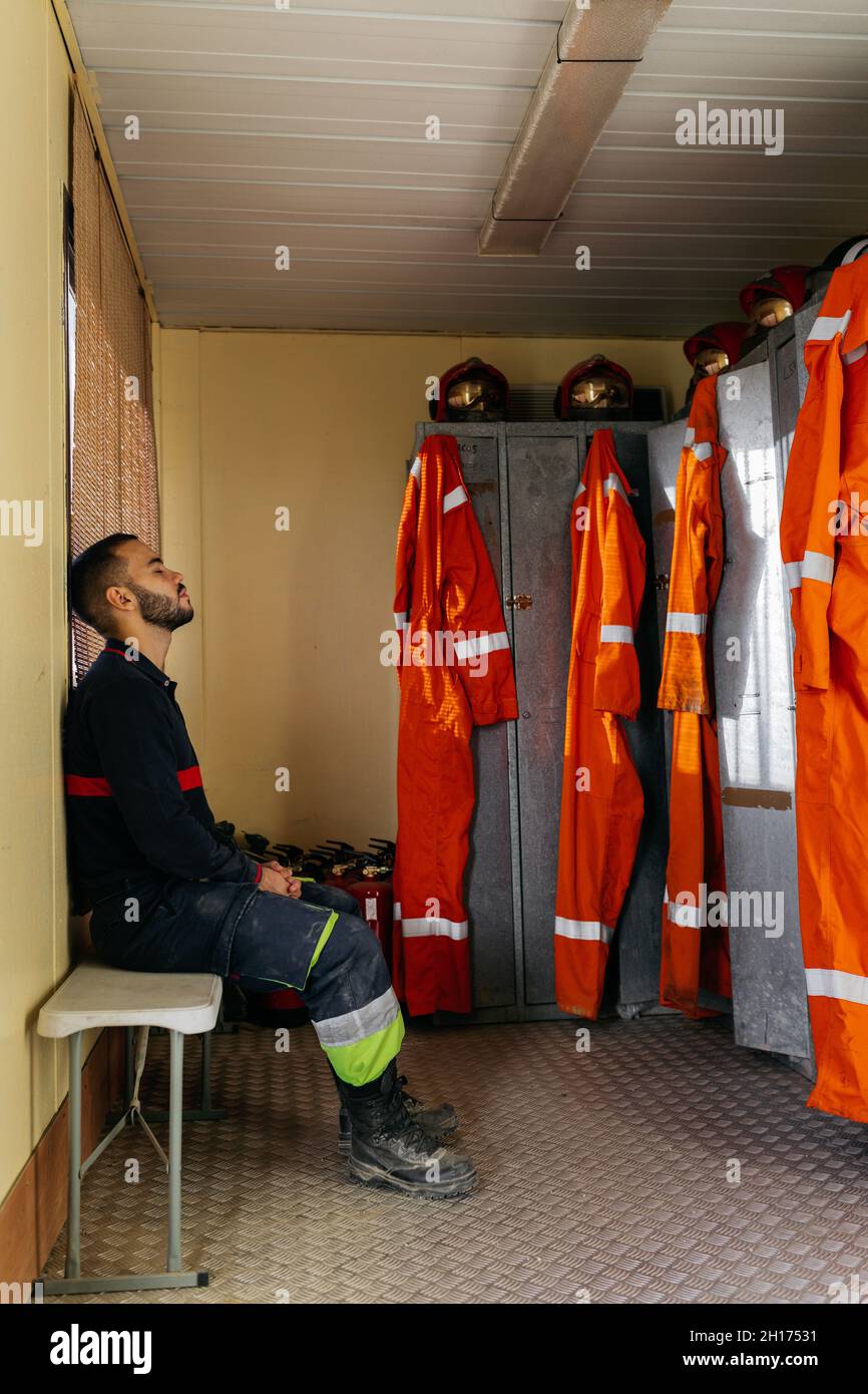 Full body side view of tired young male firefighter in uniform leaning ...