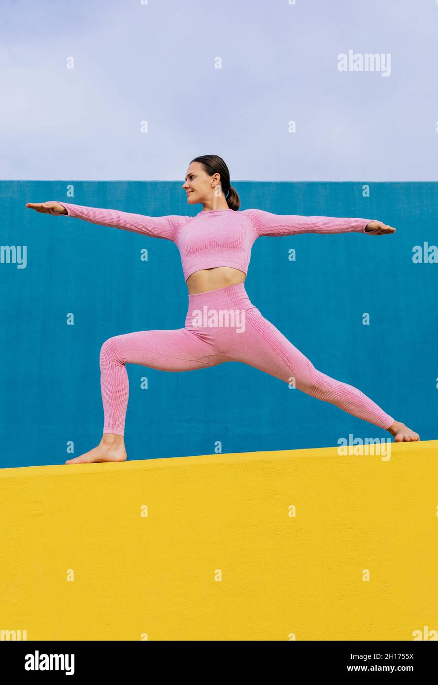 Low angle of cheerful flexible female standing in Virabhadrasana and ...