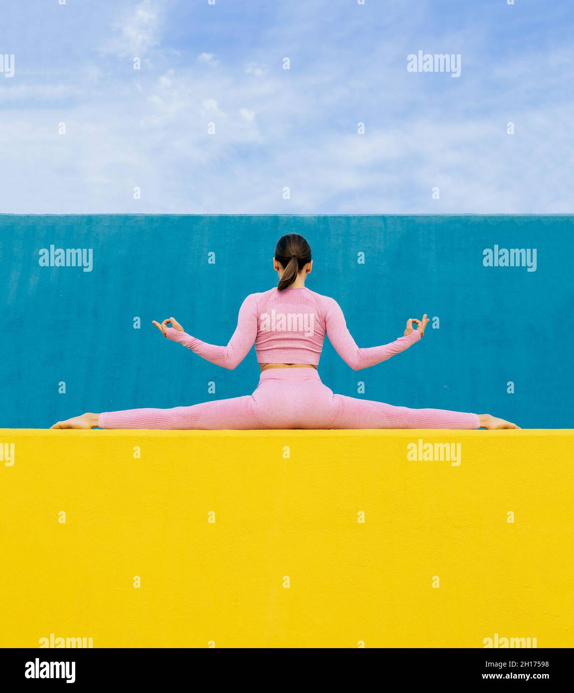 Back view of slim female sitting in split doing gyan mudra while ...