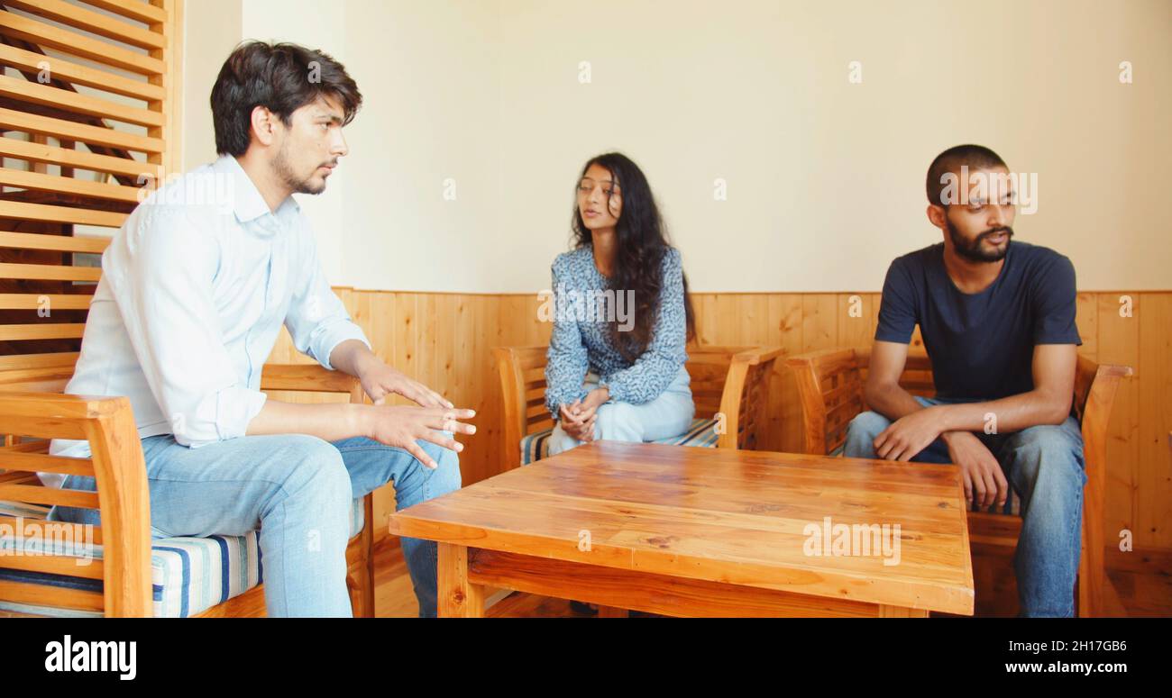 A group of Indian friends sitting in a living room, talking and ...