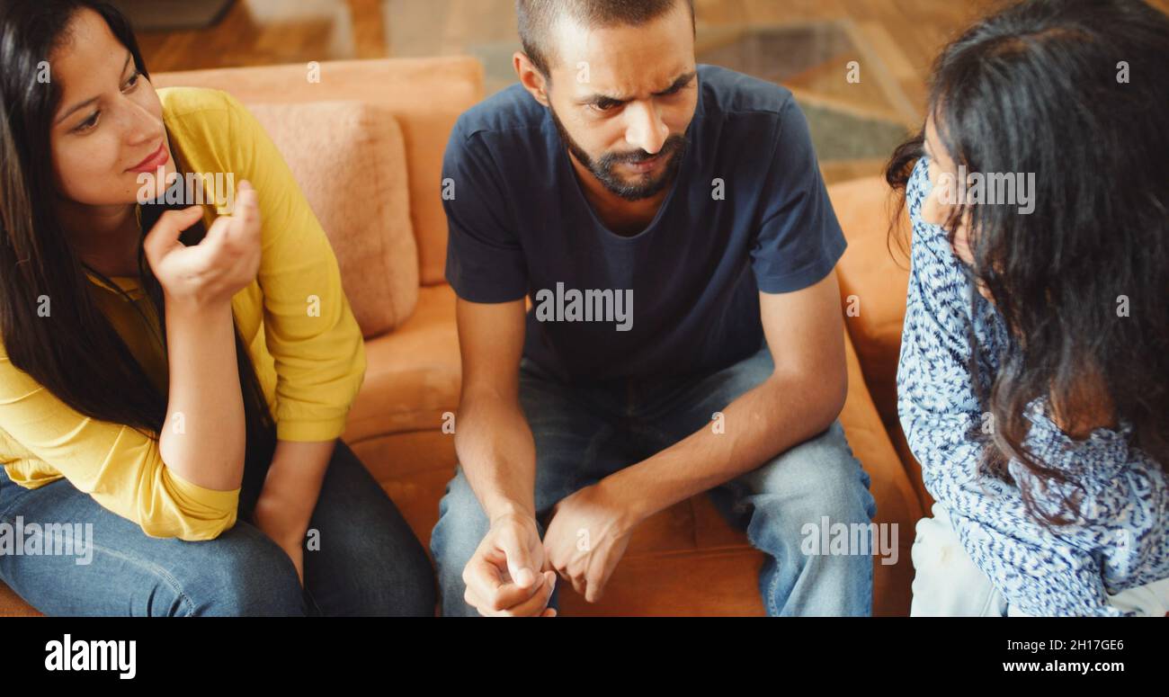 A group of Indian friends sitting in a living room, talking and ...