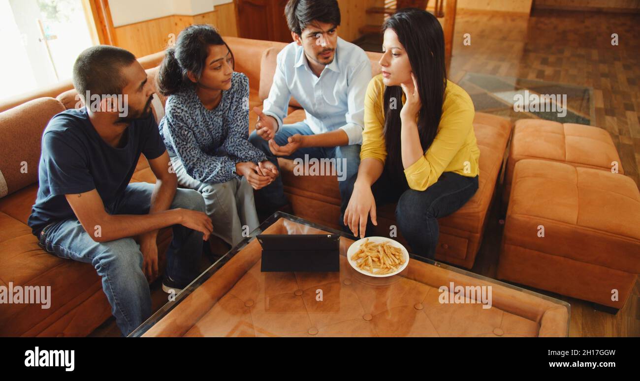 A group of Indian friends sitting in a living room, discussing a matter ...
