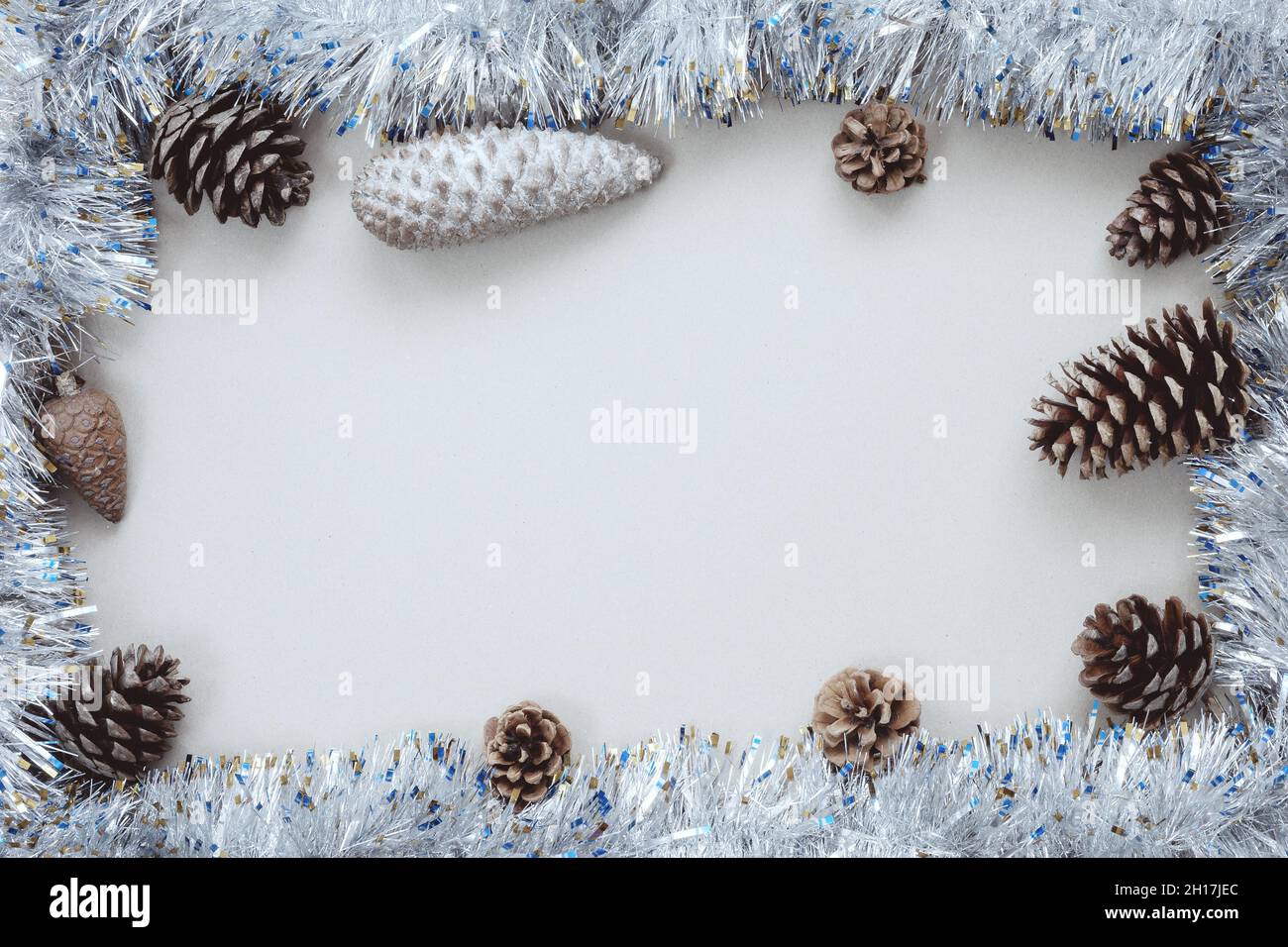 Silver tinsel with fir and pine cones frames the empty light background ...