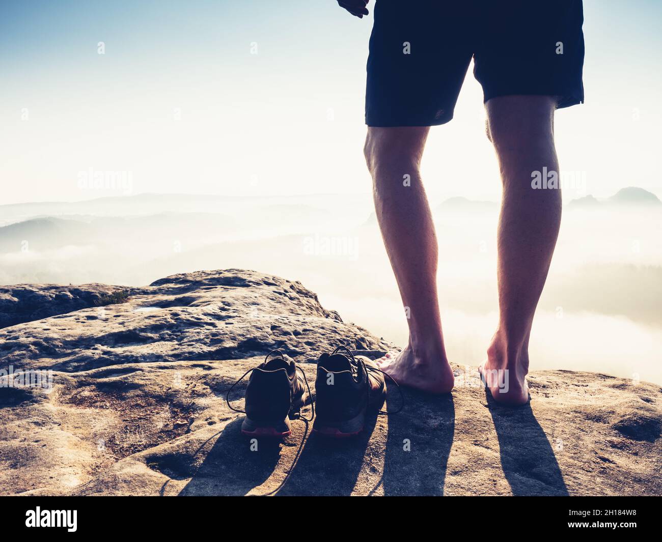 Slim male legs in strong backlight. Barefoot man hiker feet climbing on ...