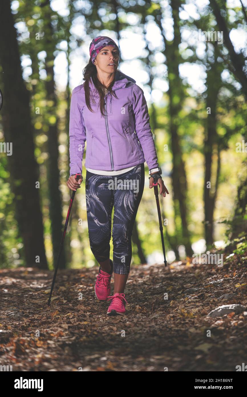 Sporty girl practicing nordic walking on the path in the forest road ...