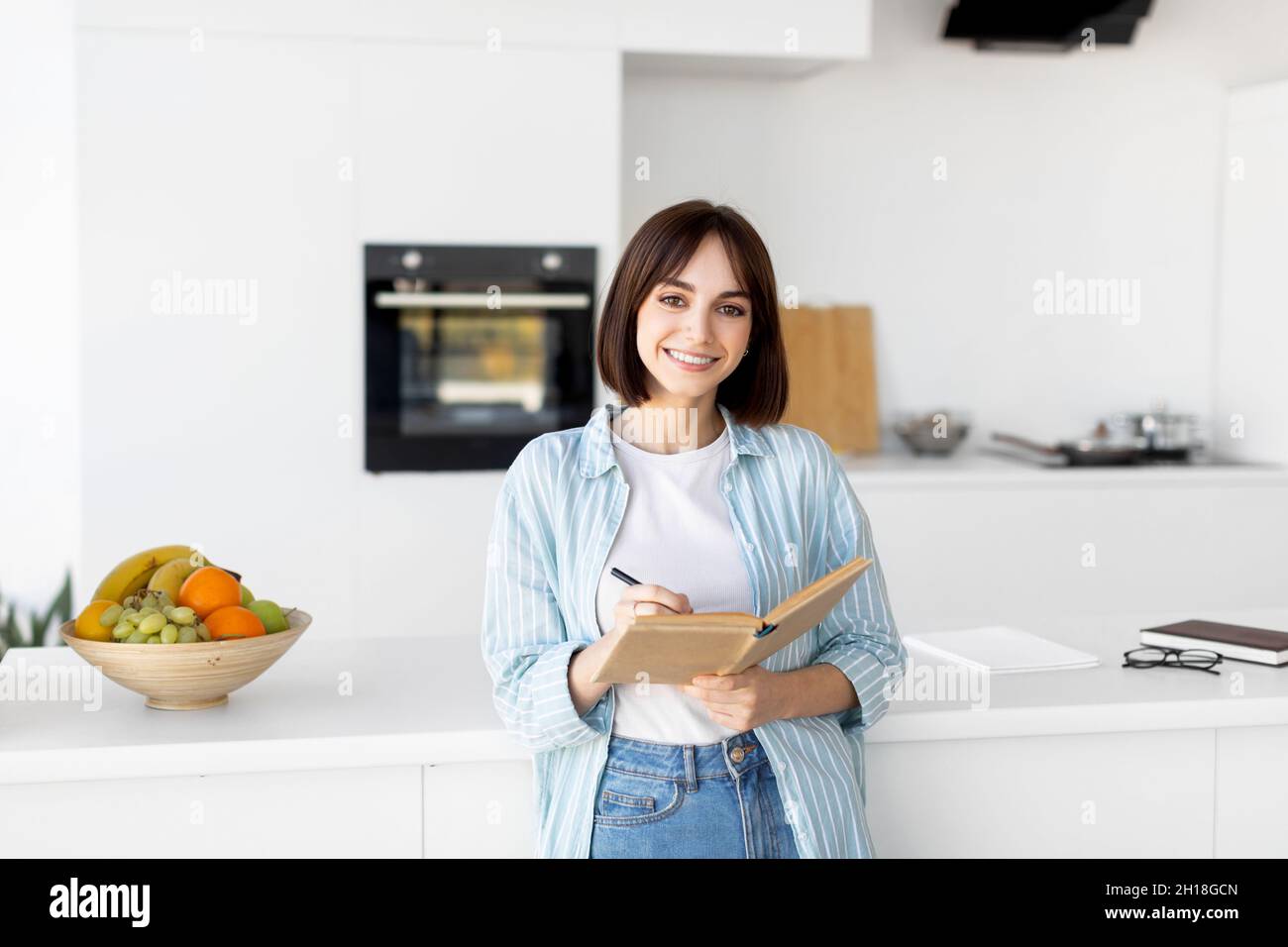Young lady smiling and taking notes, holding notepad and pen, standing ...