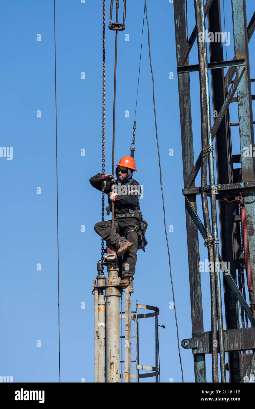 A well service hand on top of a hydraulic pumping unit prepares to ...