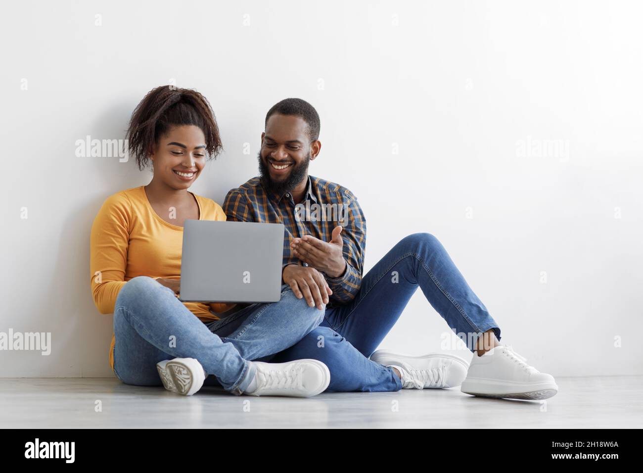 Happy millennial African American husband and wife use laptop to planning new interior design ...