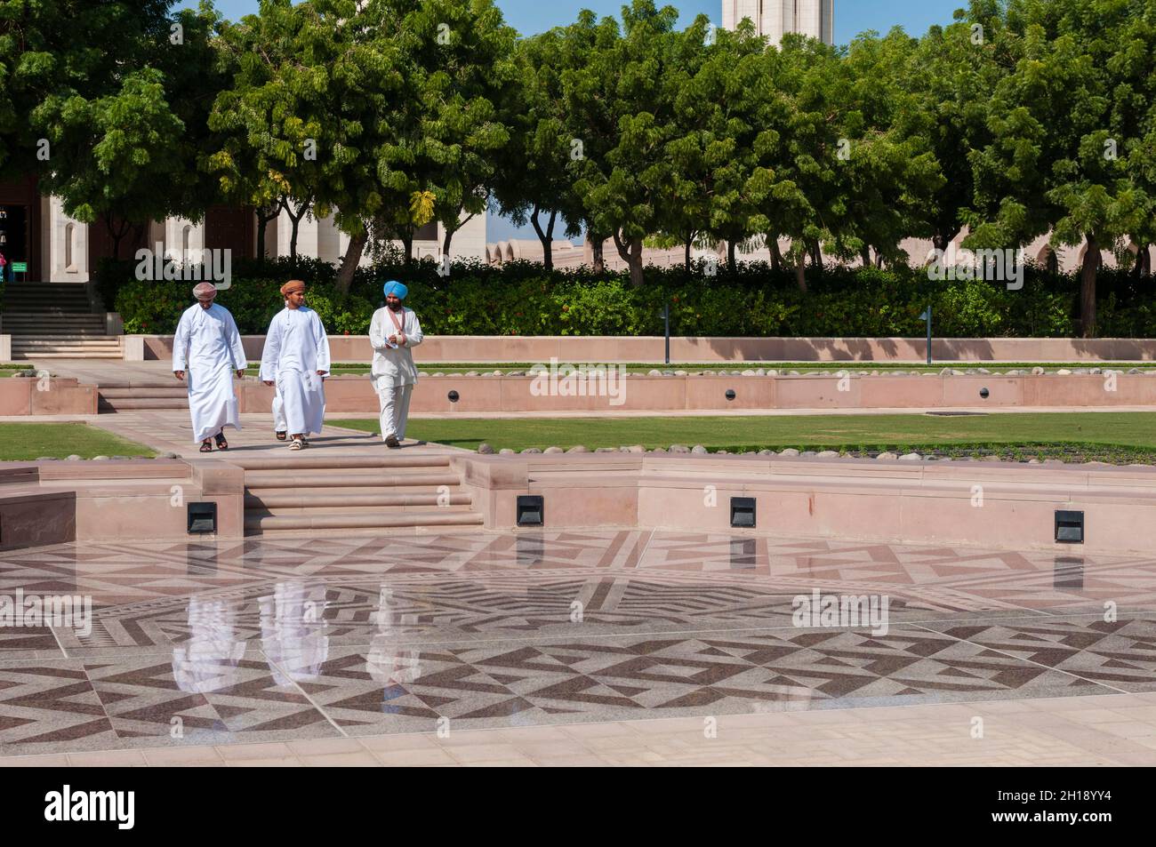 Three men walking in a courtyard at Sultan Qaboos Grand Mosque. Sultan ...