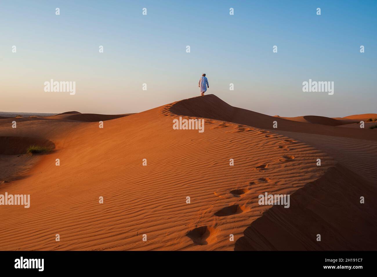An Omani man walking along a sand dune ridge at sunset. Wahiba Sands ...