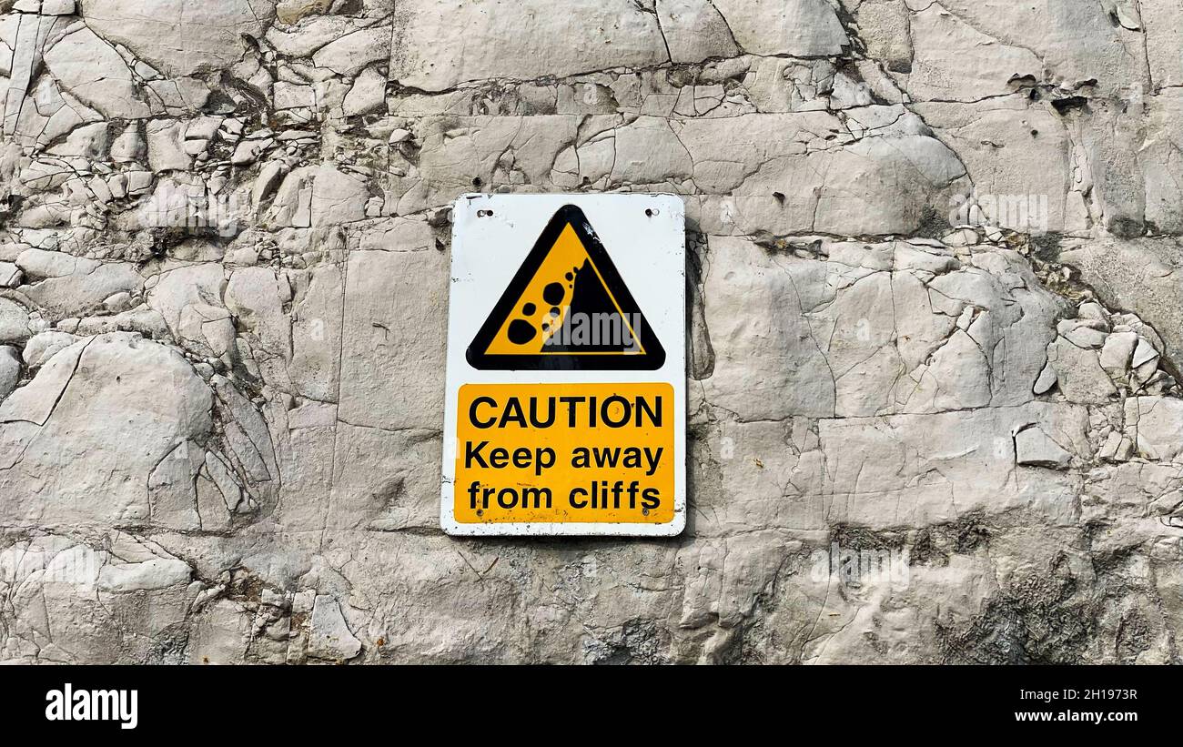 A yellow, triangle caution sign about rock slide attached to a cliff ...