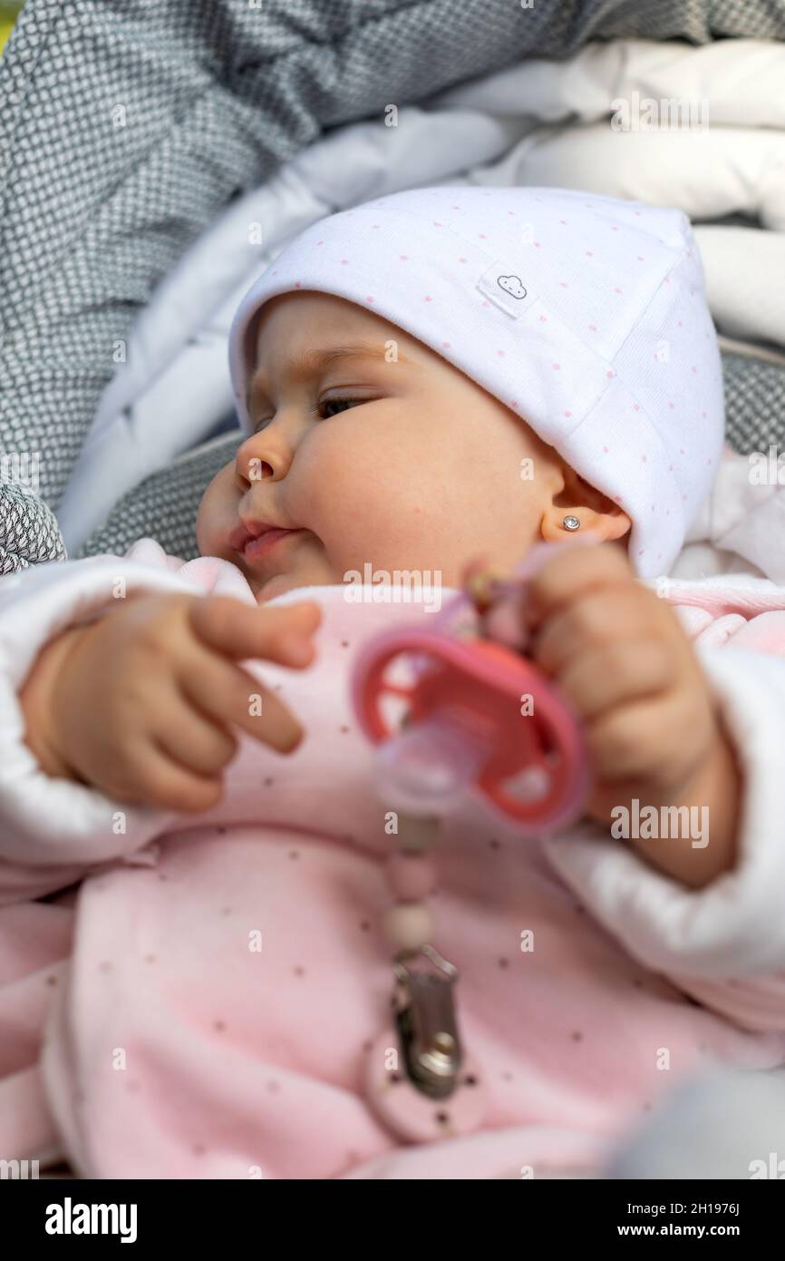 Baby girl with a pacifier in his mouth sitting in a stroller outdoor ...