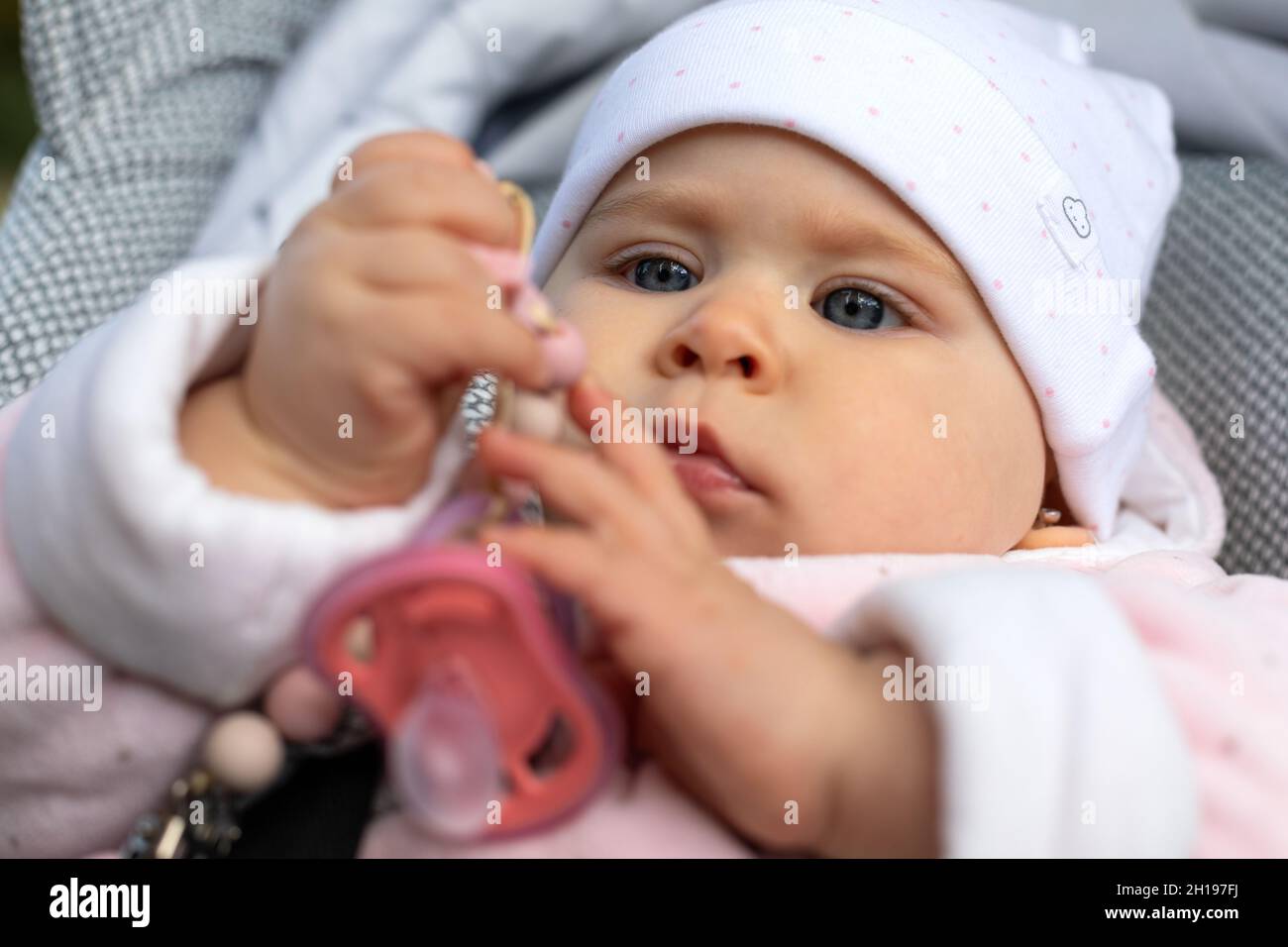 Baby girl with a pacifier in his mouth sitting in a stroller outdoor ...