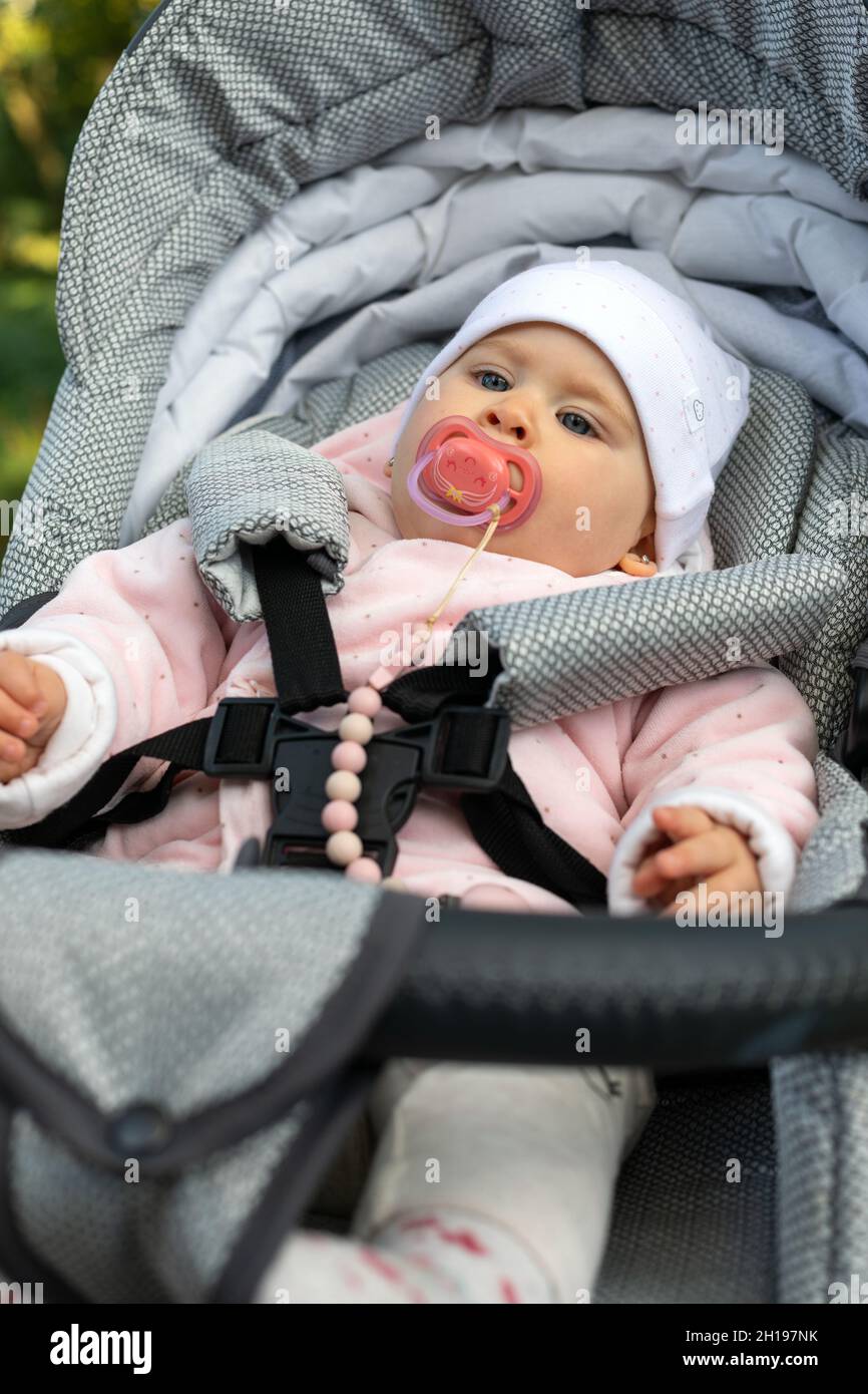 Baby girl with a pacifier in his mouth sitting in a stroller outdoor ...