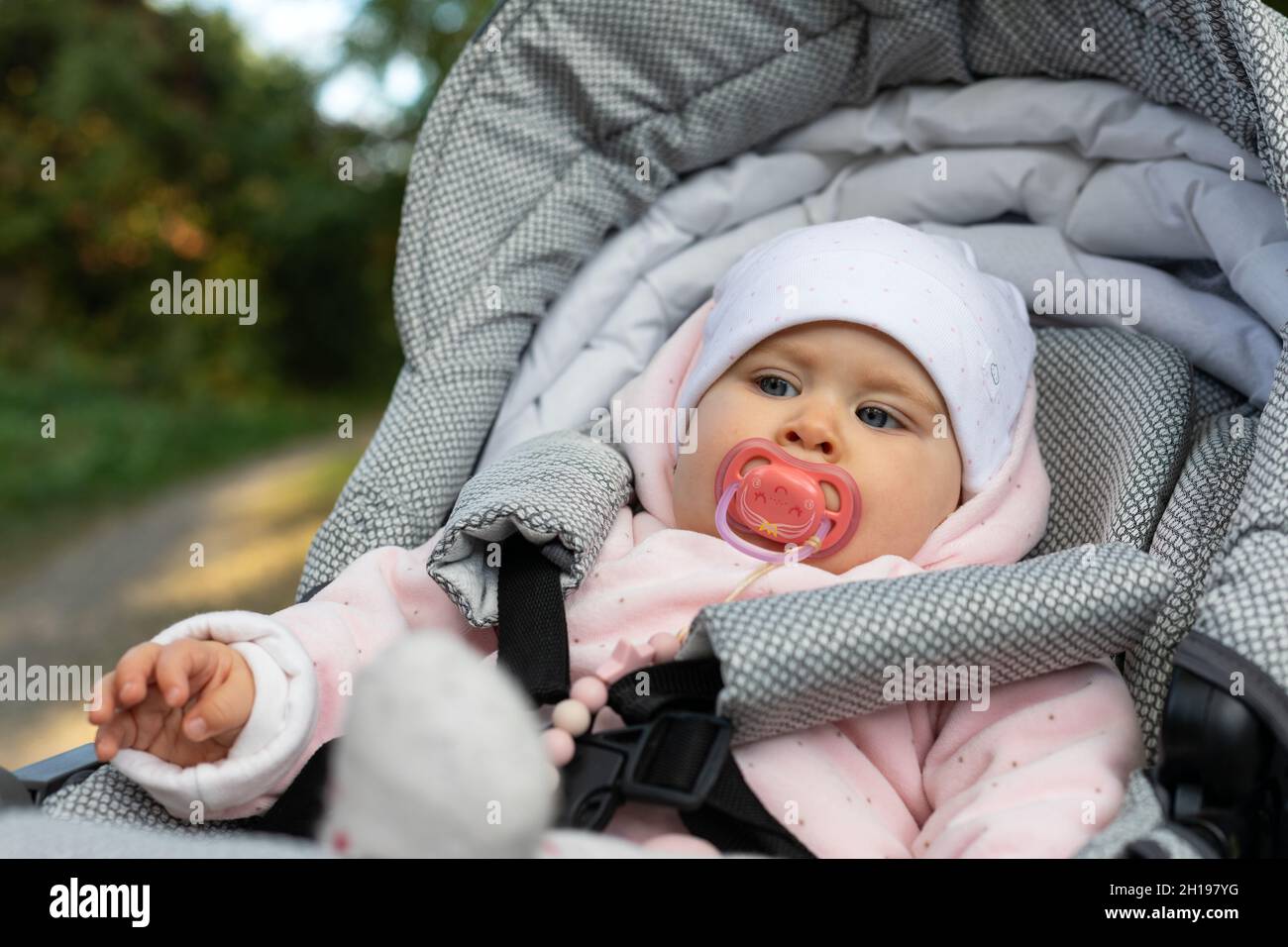 Baby girl with a pacifier in his mouth sitting in a stroller outdoor ...
