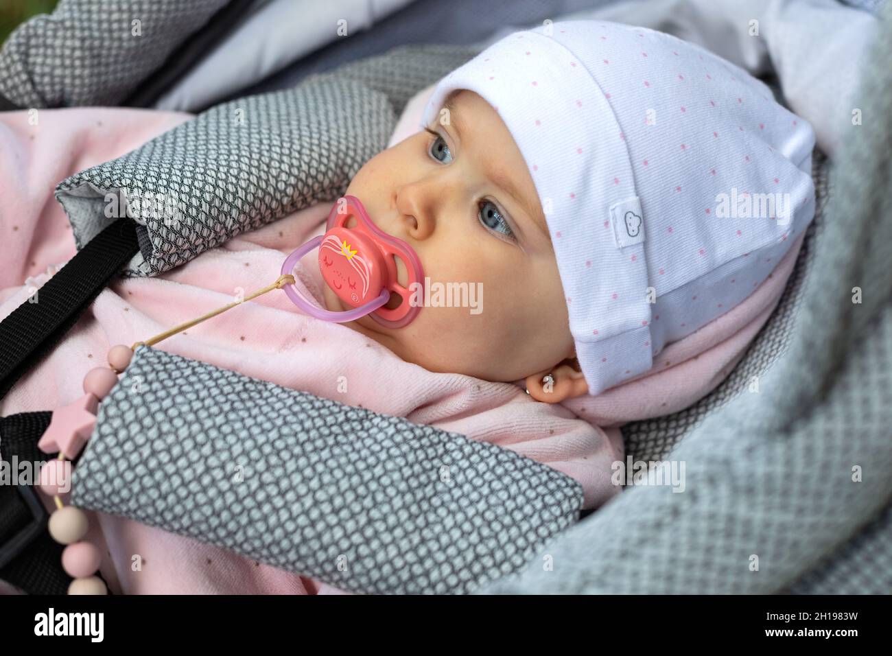 Baby girl with a pacifier in his mouth sitting in a stroller outdoor ...