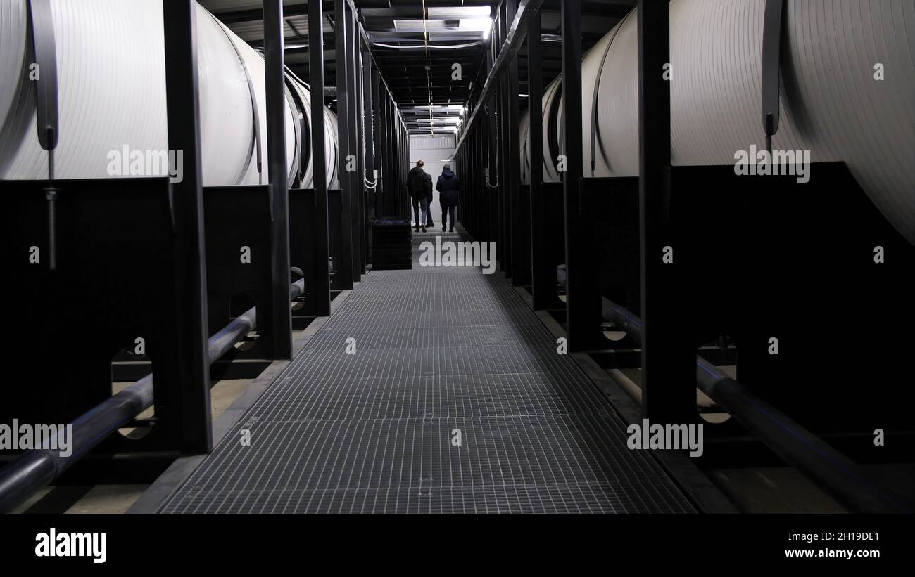 Rear view of three men walking along water treatment tanks at the power ...